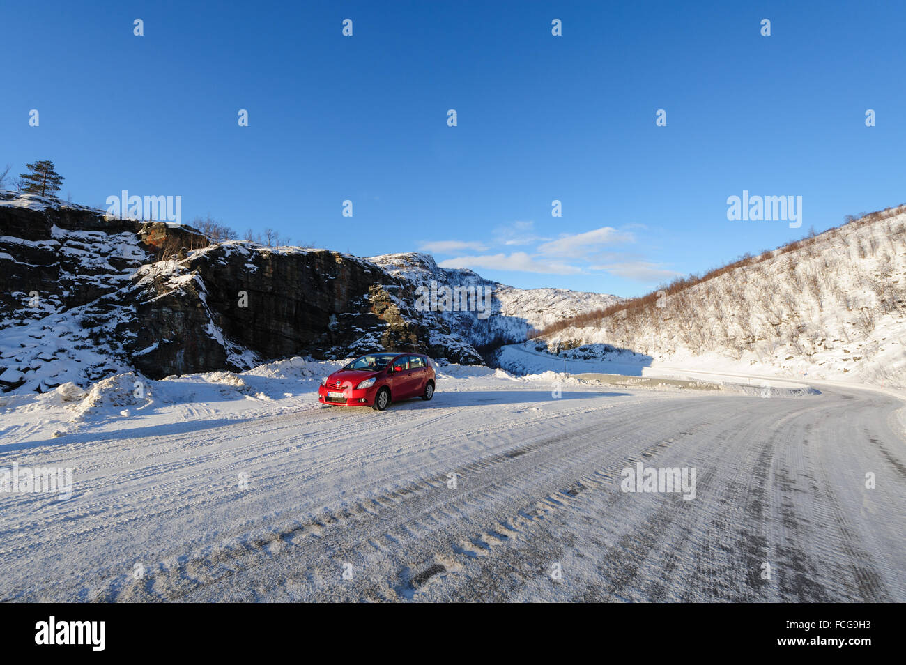 Ice on a road in northern Norway with a red car parked along the road ...
