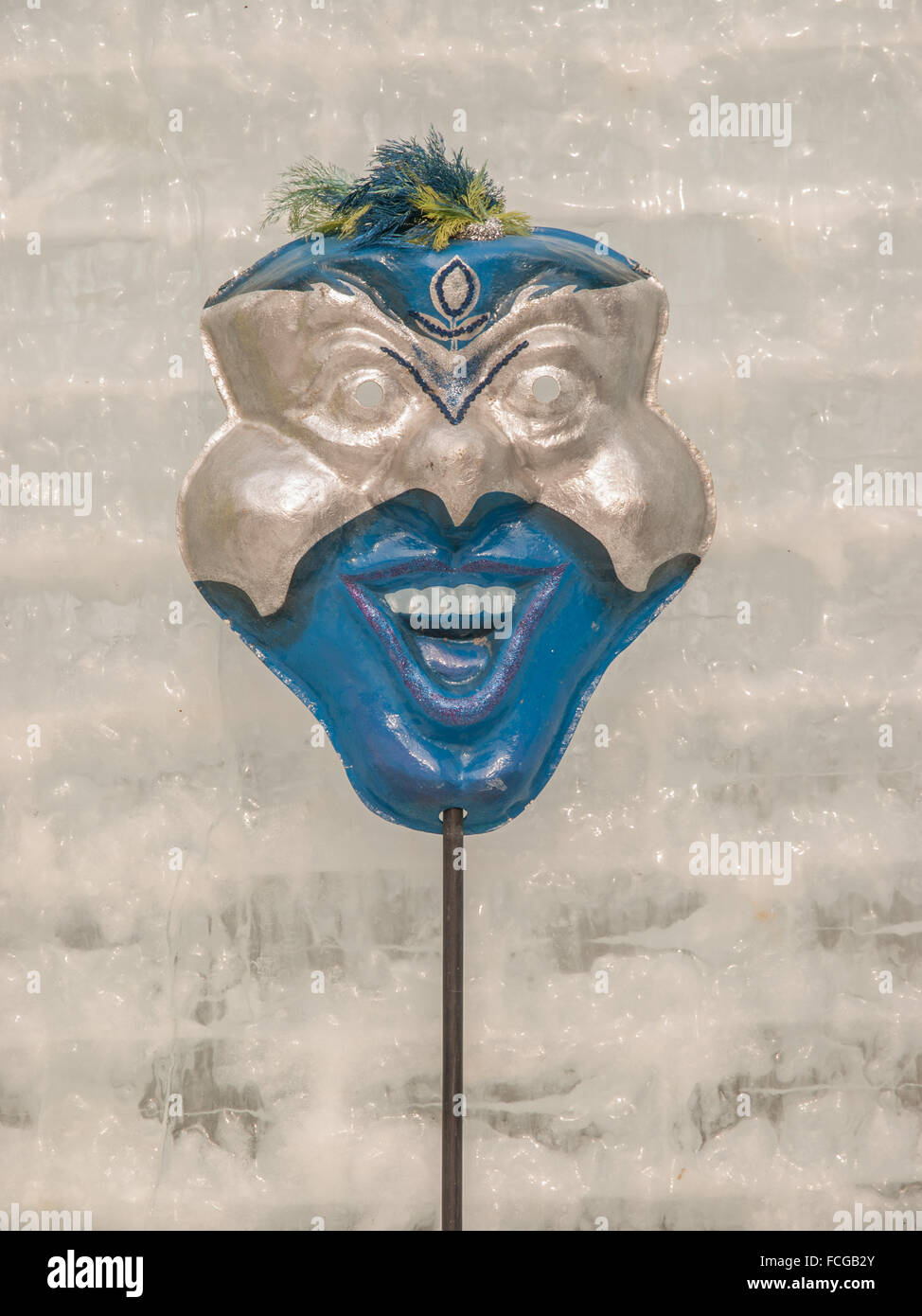 Colourful mask on pole in front of a brick wall made of ice at Carnaval ...