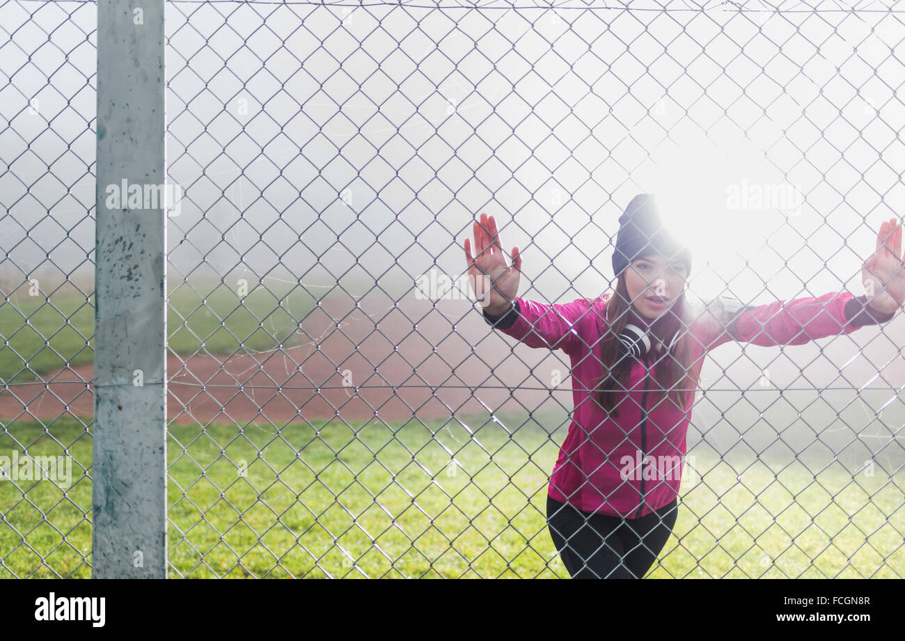 Young woman standing behind mesh wire fence doing stretching exercises ...