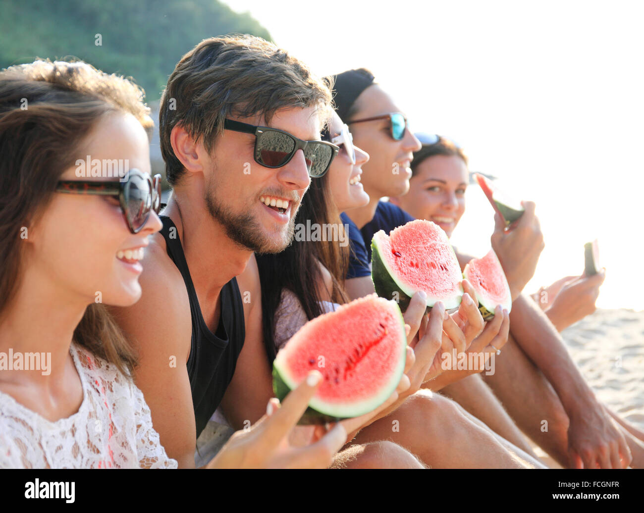 Happy young friends eating watermelon on beach Stock Photo - Alamy