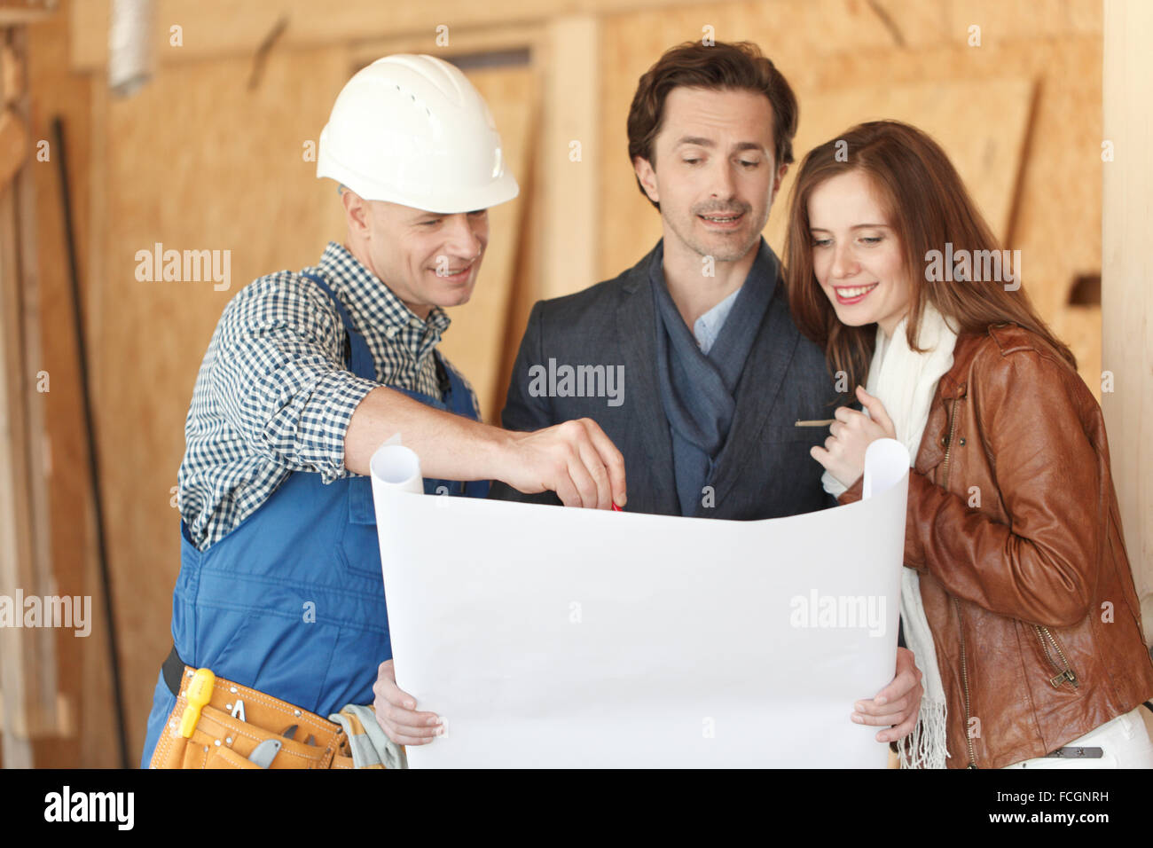 Worker shows house design plans to a young couple at construction site ...