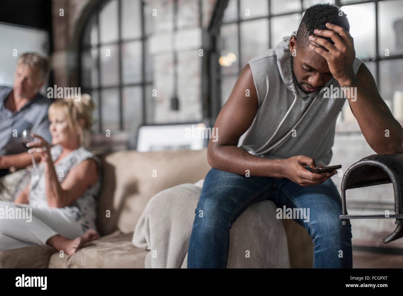 Young man sitting on couch cellphone looking worried Stock Photo - Alamy