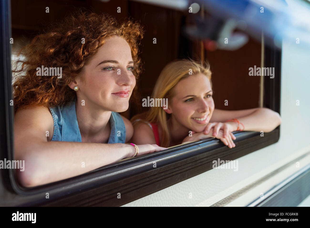 Two female friends looking through window of caravan watching something ...