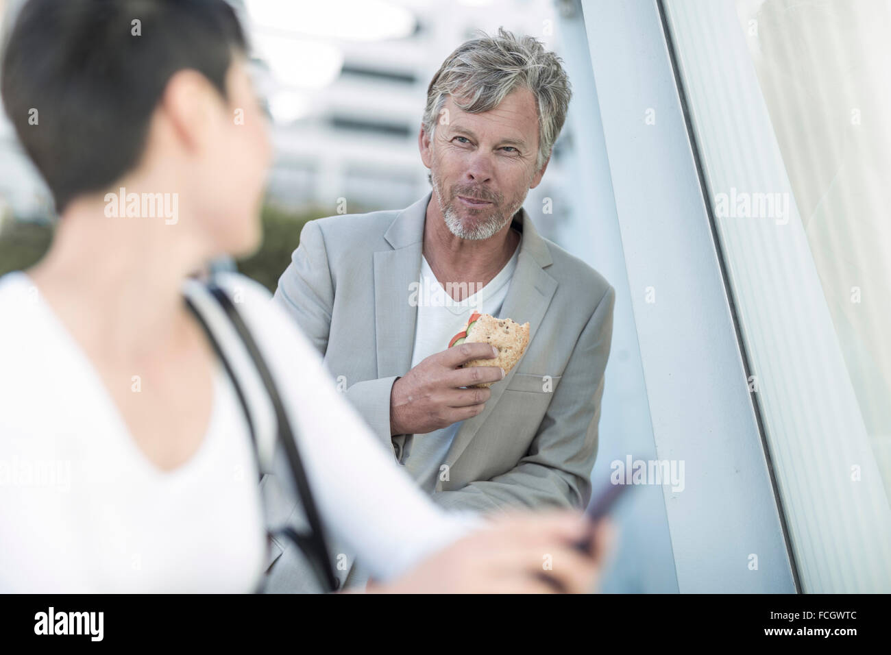 Mature man eating sandwich talking to young woman Stock Photo - Alamy