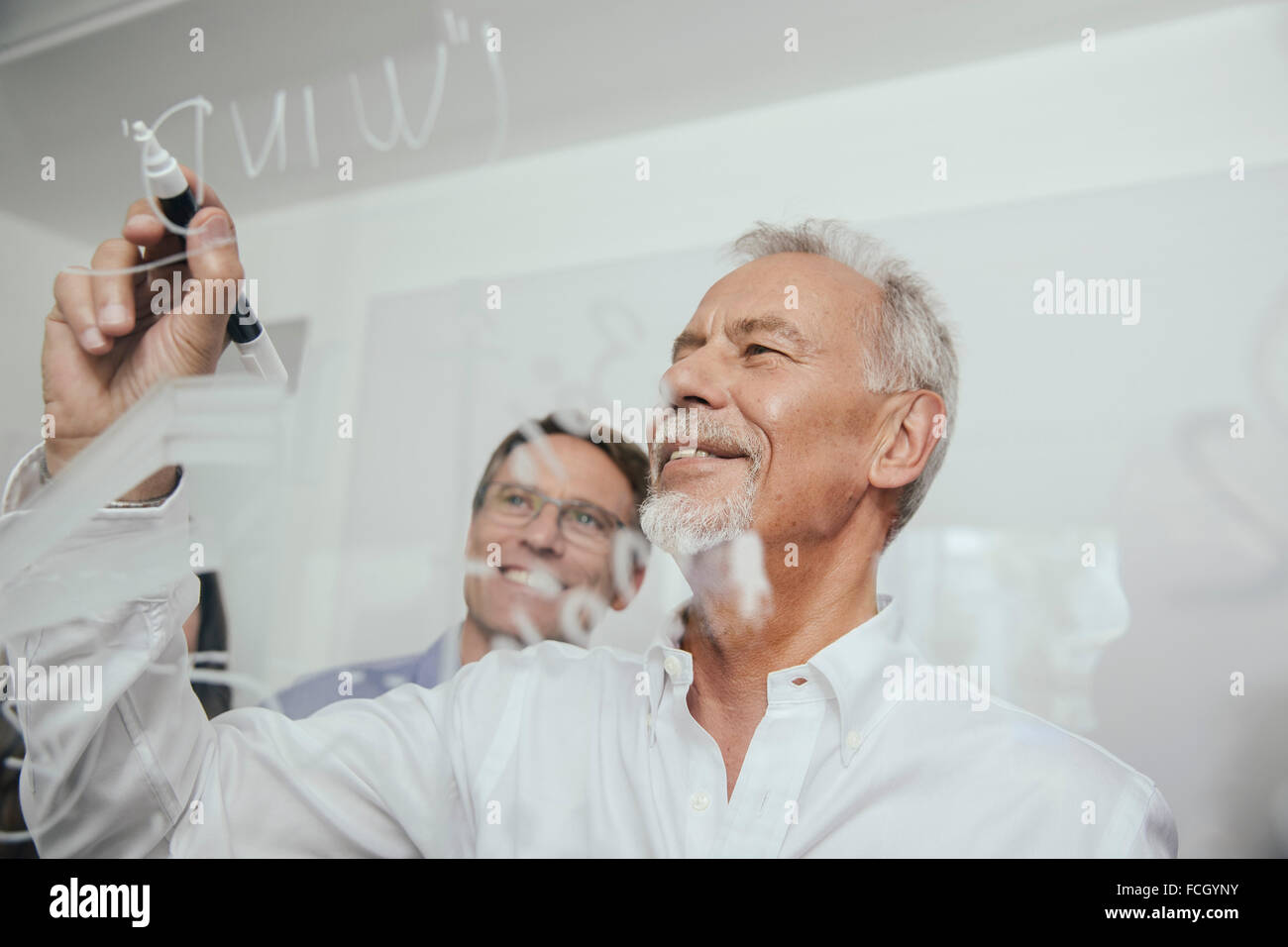 Two men writing onto glass wall in office Stock Photo - Alamy