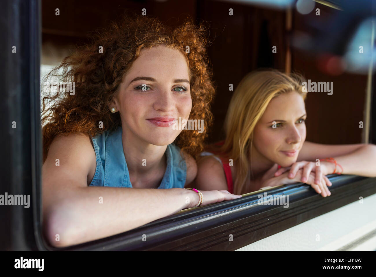 Two female friends looking through window of caravan Stock Photo - Alamy