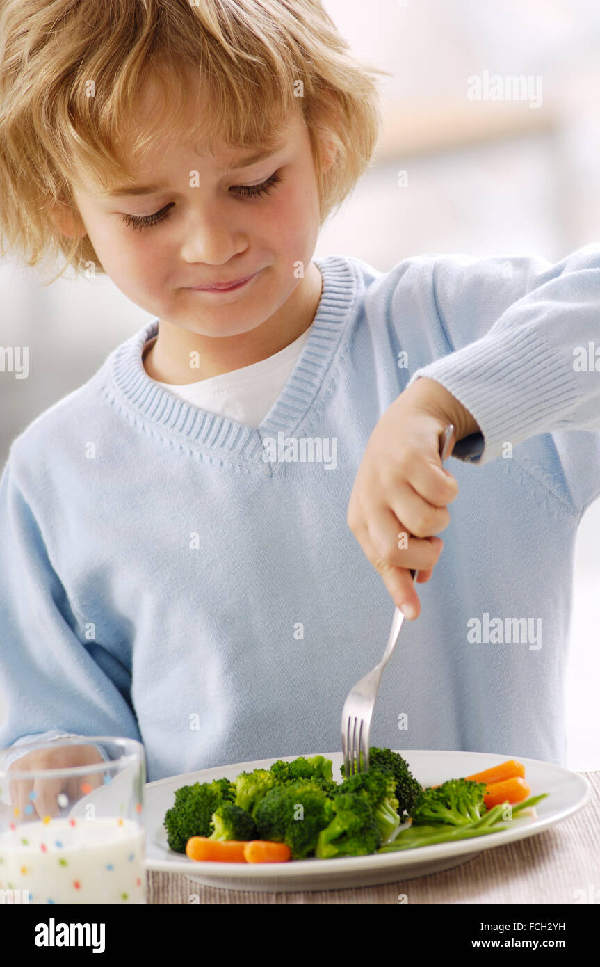 Portrait of smiling blond boy eating broccoli Stock Photo - Alamy