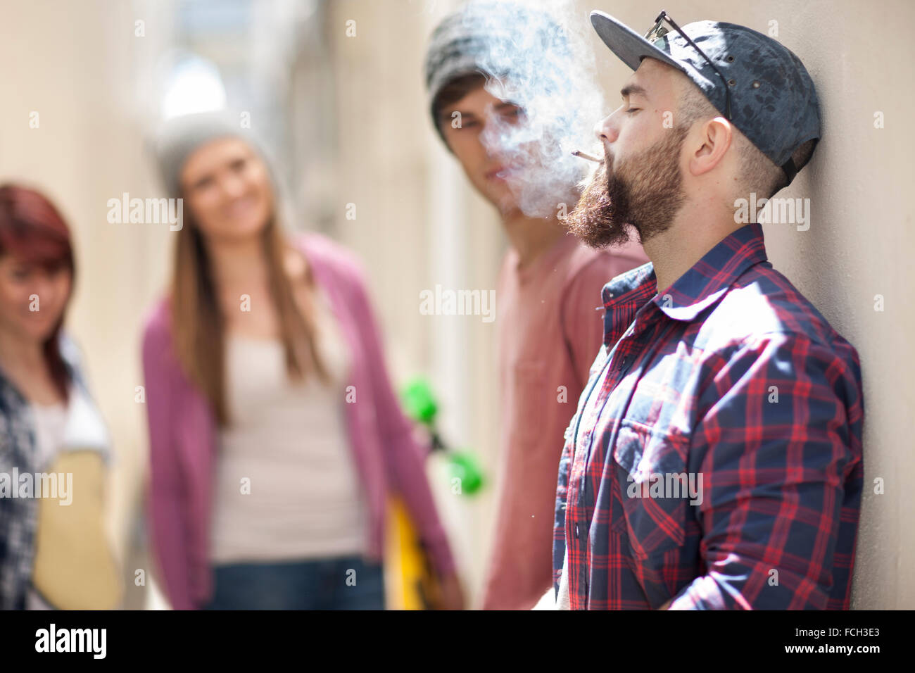 Young man smoking a cigarette friends in background Stock Photo - Alamy