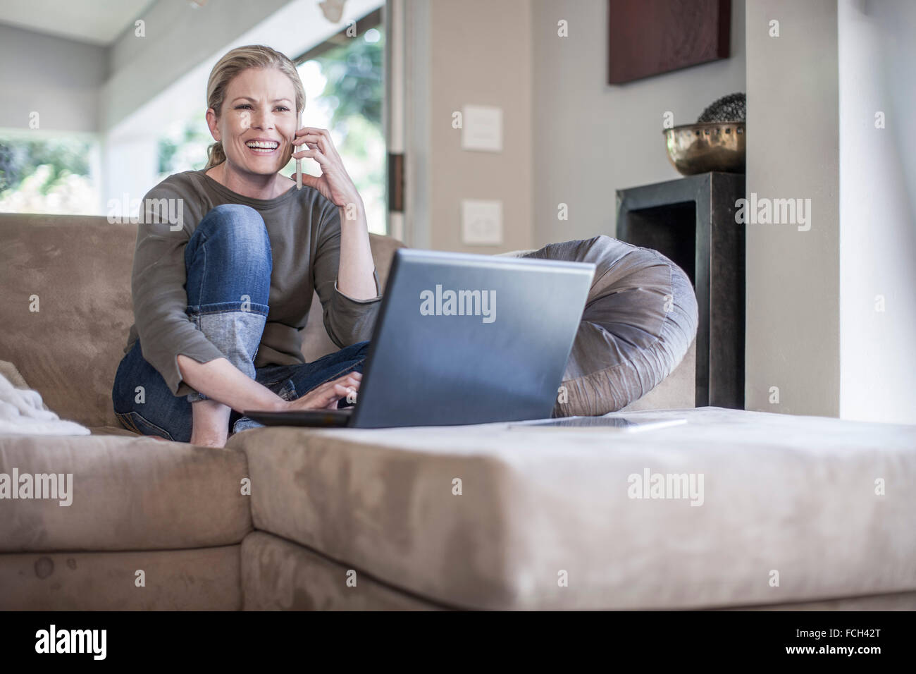 Woman sitting on couch cell phone and laptop Stock Photo - Alamy