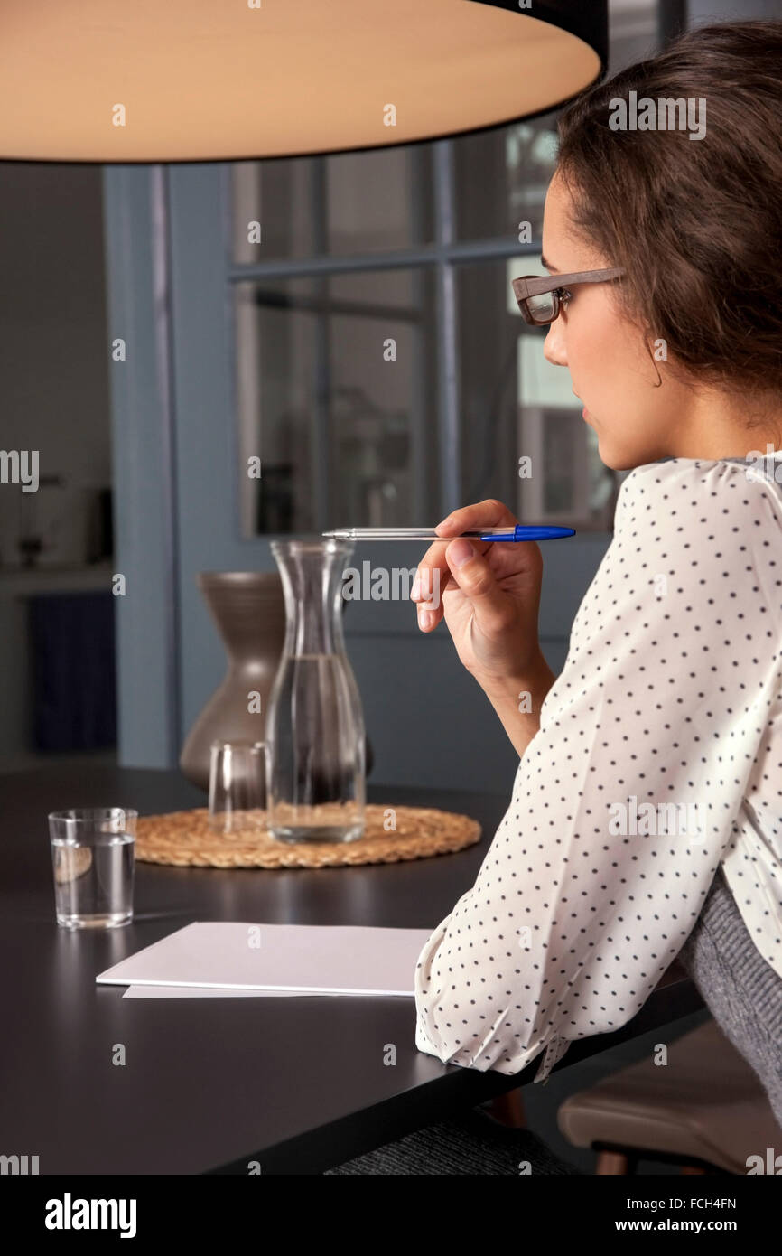 Young woman sitting at table about to write on paper Stock Photo - Alamy