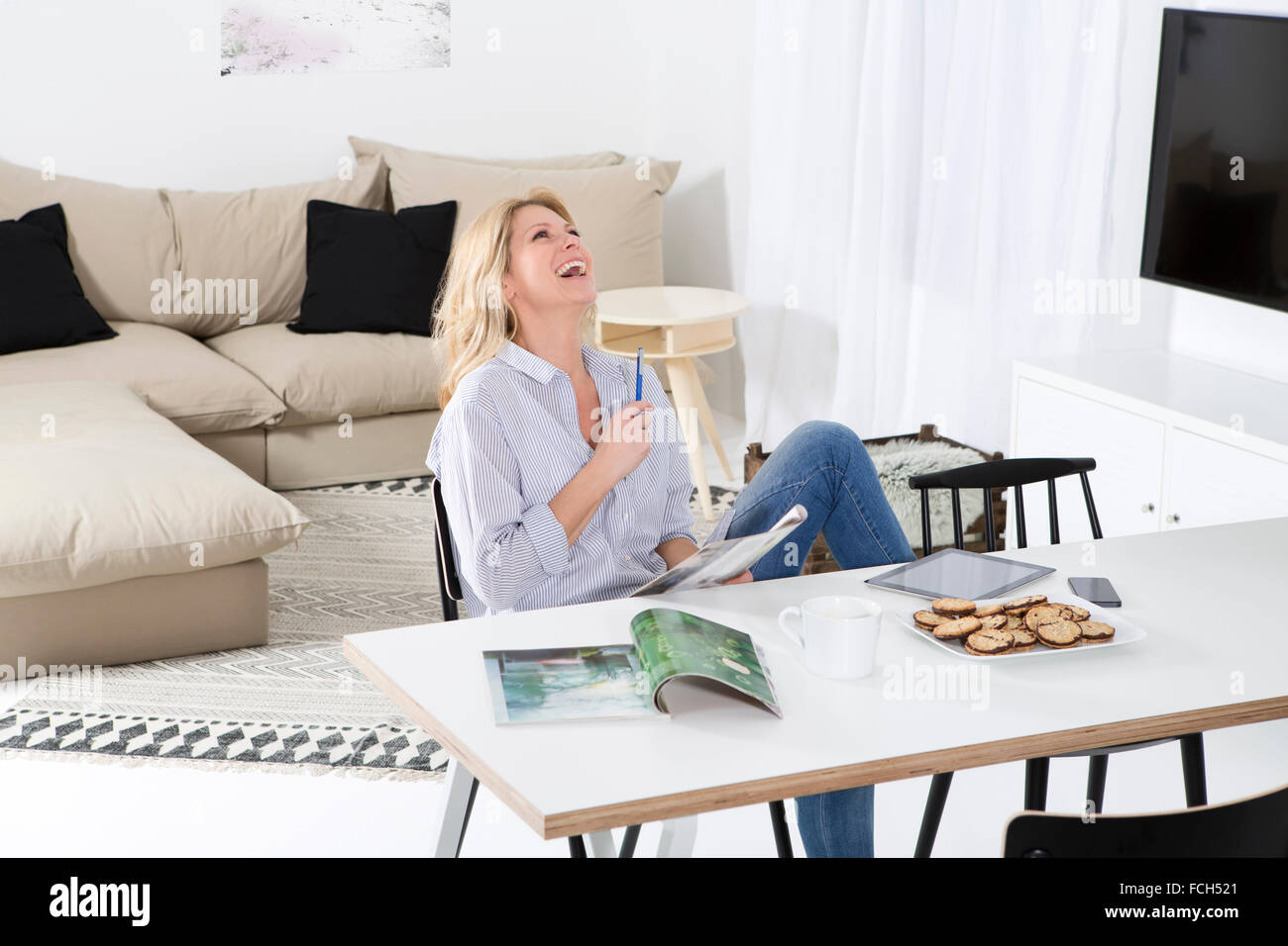 Laughing woman sitting at the table in her living room magazine Stock ...