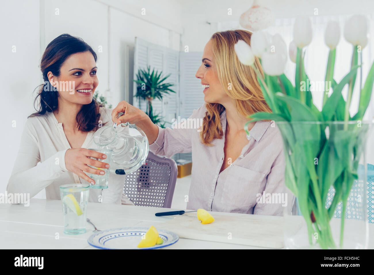 Woman pouring water in a glass of her female friend while sitting at ...