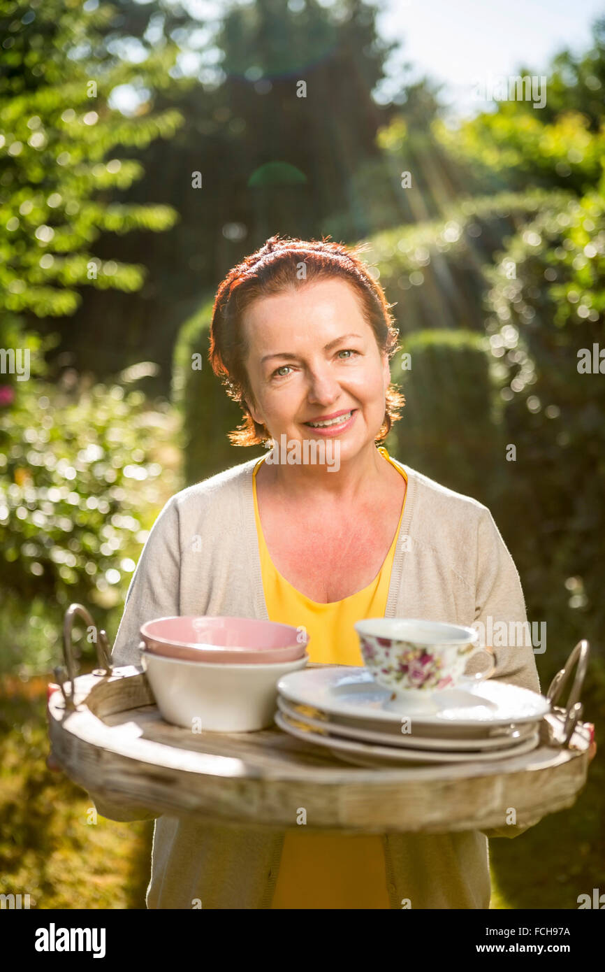 Mature woman carrying tray dish set in garden Stock Photo - Alamy