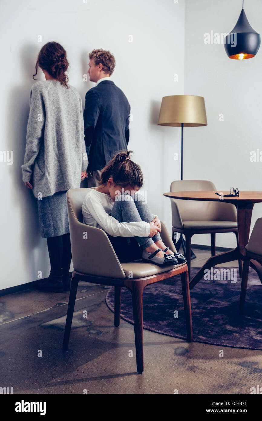 Sad girl sitting on a chair her parents standing at a wall Stock Photo ...