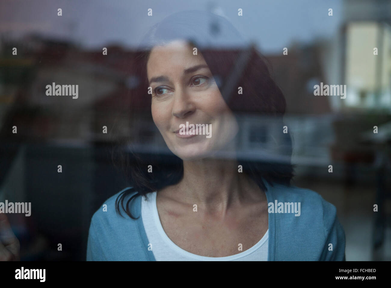 Smiling woman behind windowpane looking out Stock Photo - Alamy