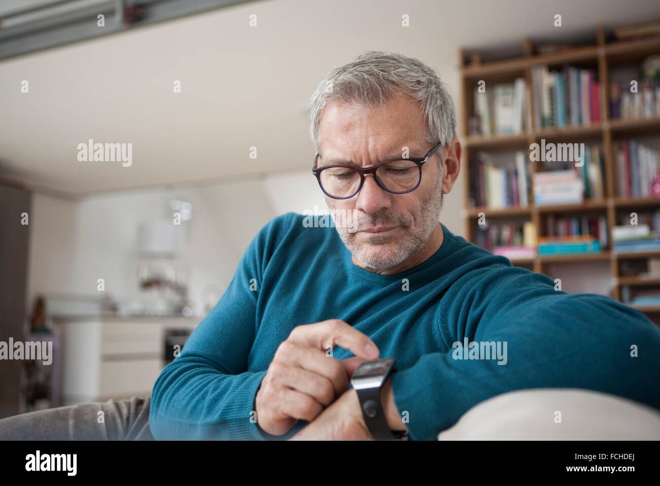 Man at home sitting on couch looking at watch Stock Photo - Alamy