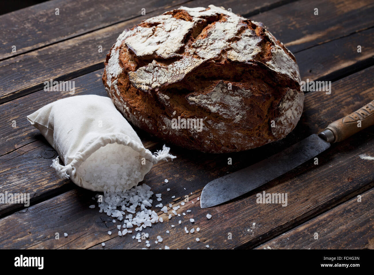 Crusty bread bread knife and sachet of salt grains on dark wood Stock ...