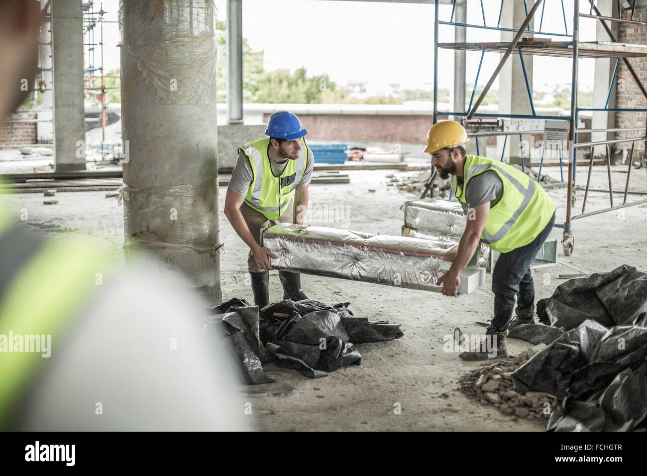 Two construction workers carrying item in construction site Stock Photo ...