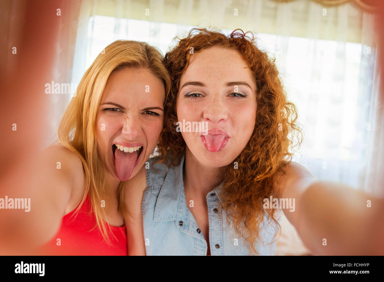 Portrait Of Two Female Friends Sticking Out Tongues While Looking At