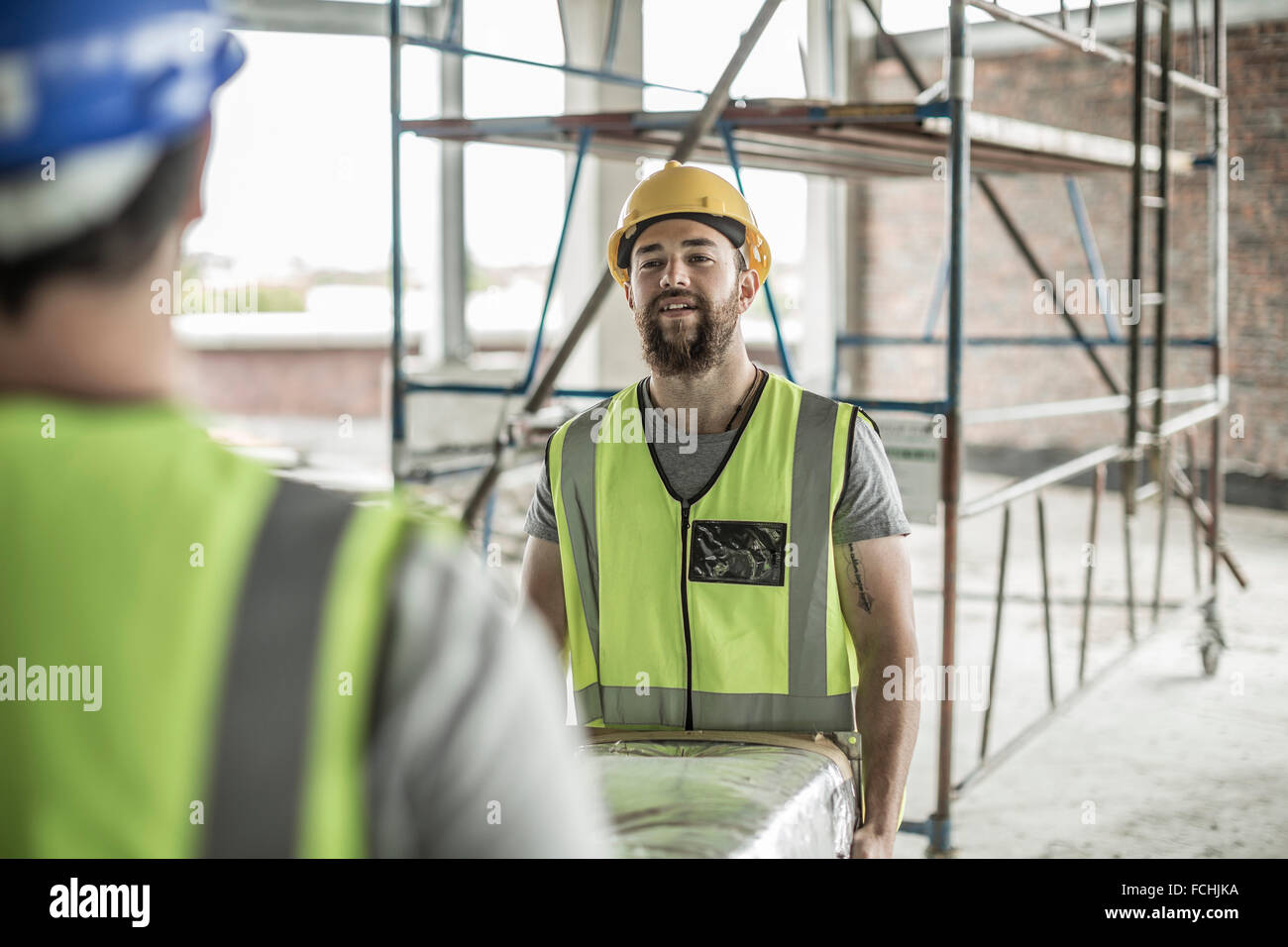 Two construction workers carrying item in construction site Stock Photo ...