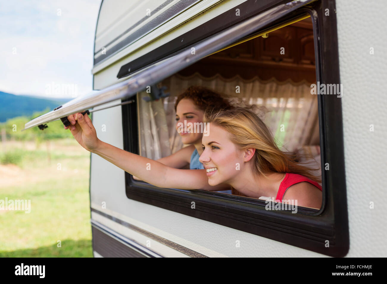 Two female friends looking through window of caravan Stock Photo - Alamy
