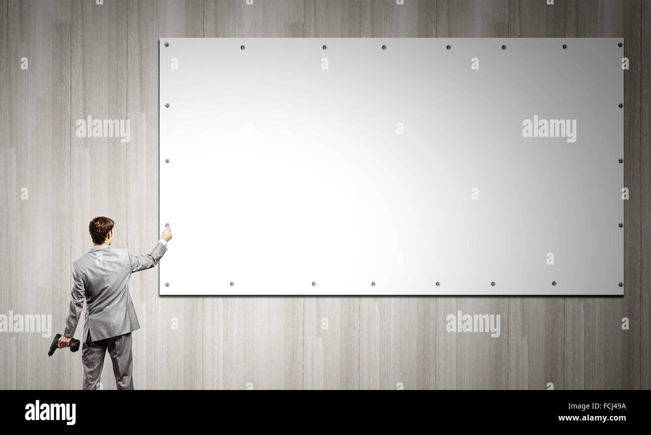 Rear view of businessman fixing blank white banner on wall Stock Photo ...
