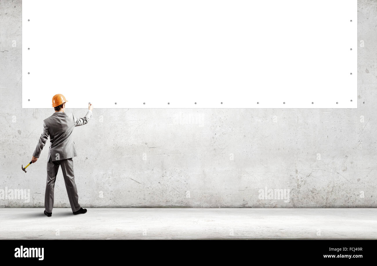 Rear view of businessman fixing blank white banner on wall Stock Photo ...