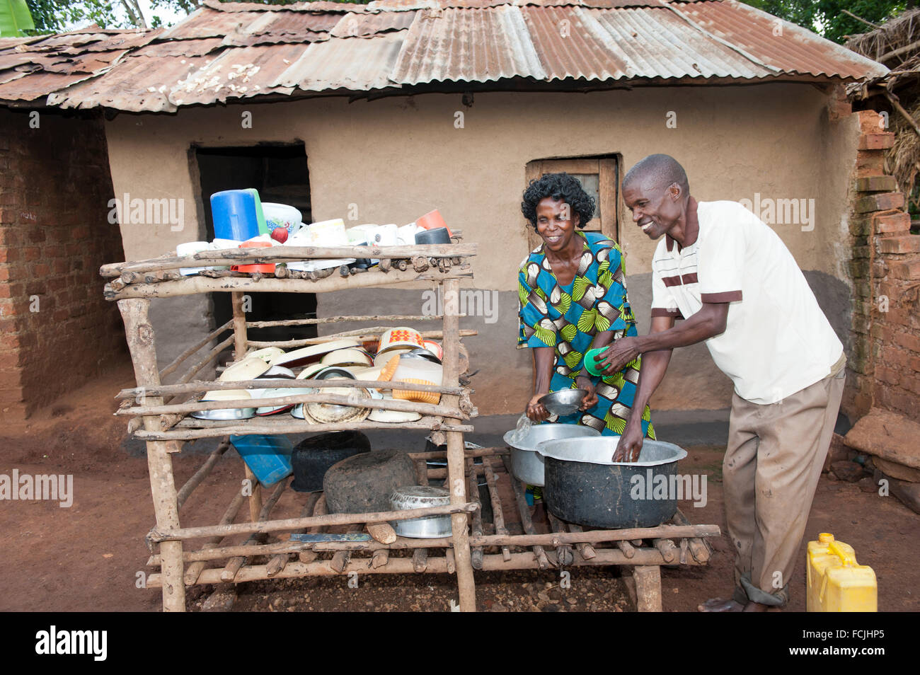 Ugandan couple working together to clean dishes in a rural village ...