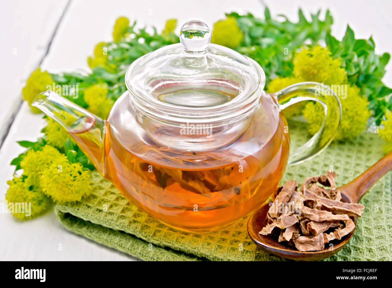 Herbal tea in a glass teapot on a napkin, spoon with dry roots of ...