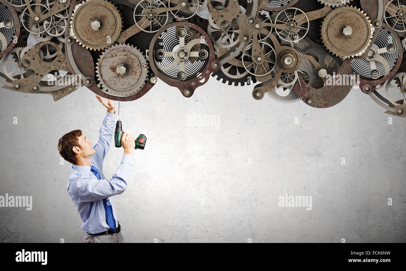Young businessman using drill to fix gear mechanism Stock Photo - Alamy