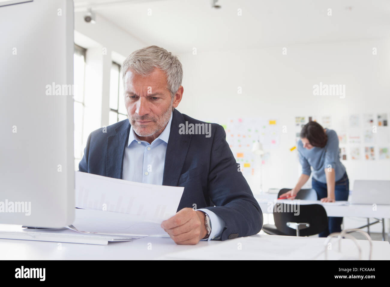 Businessman in office at desk looking at paper Stock Photo - Alamy