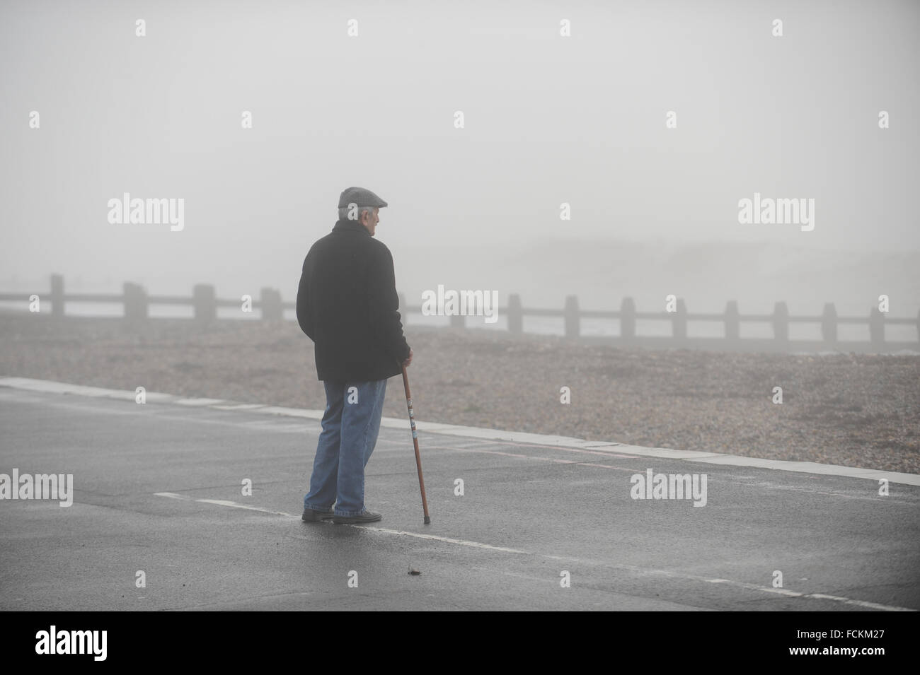 In thick fog, an old man stands on the promenade looking out to sea in ...