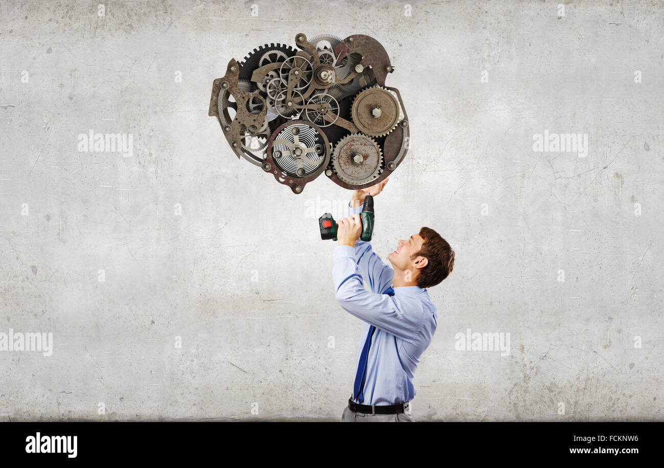 Young businessman using drill to fix gear mechanism Stock Photo - Alamy