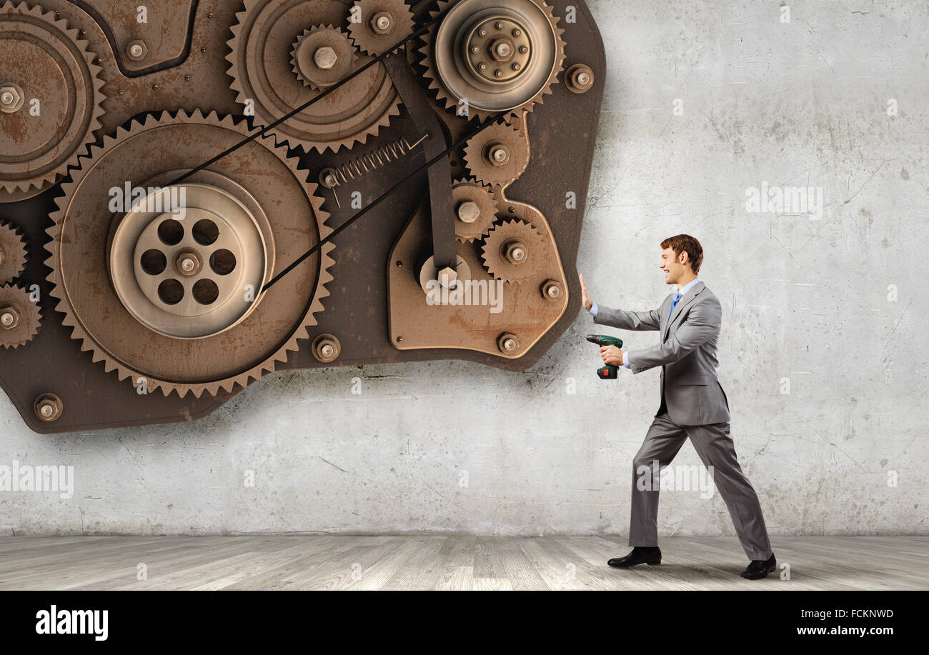 Young businessman using drill to fix gear mechanism Stock Photo - Alamy