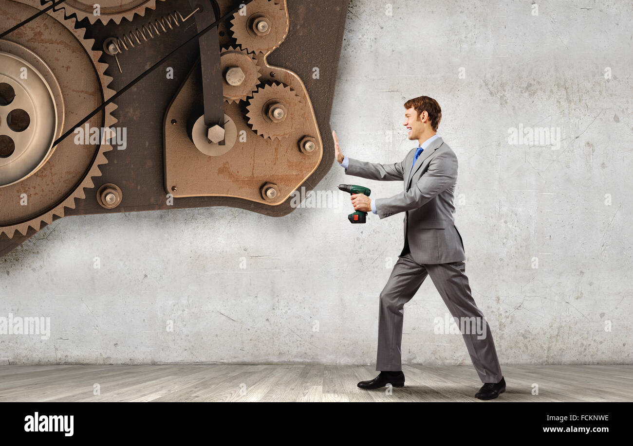 Young businessman using drill to fix gear mechanism Stock Photo - Alamy