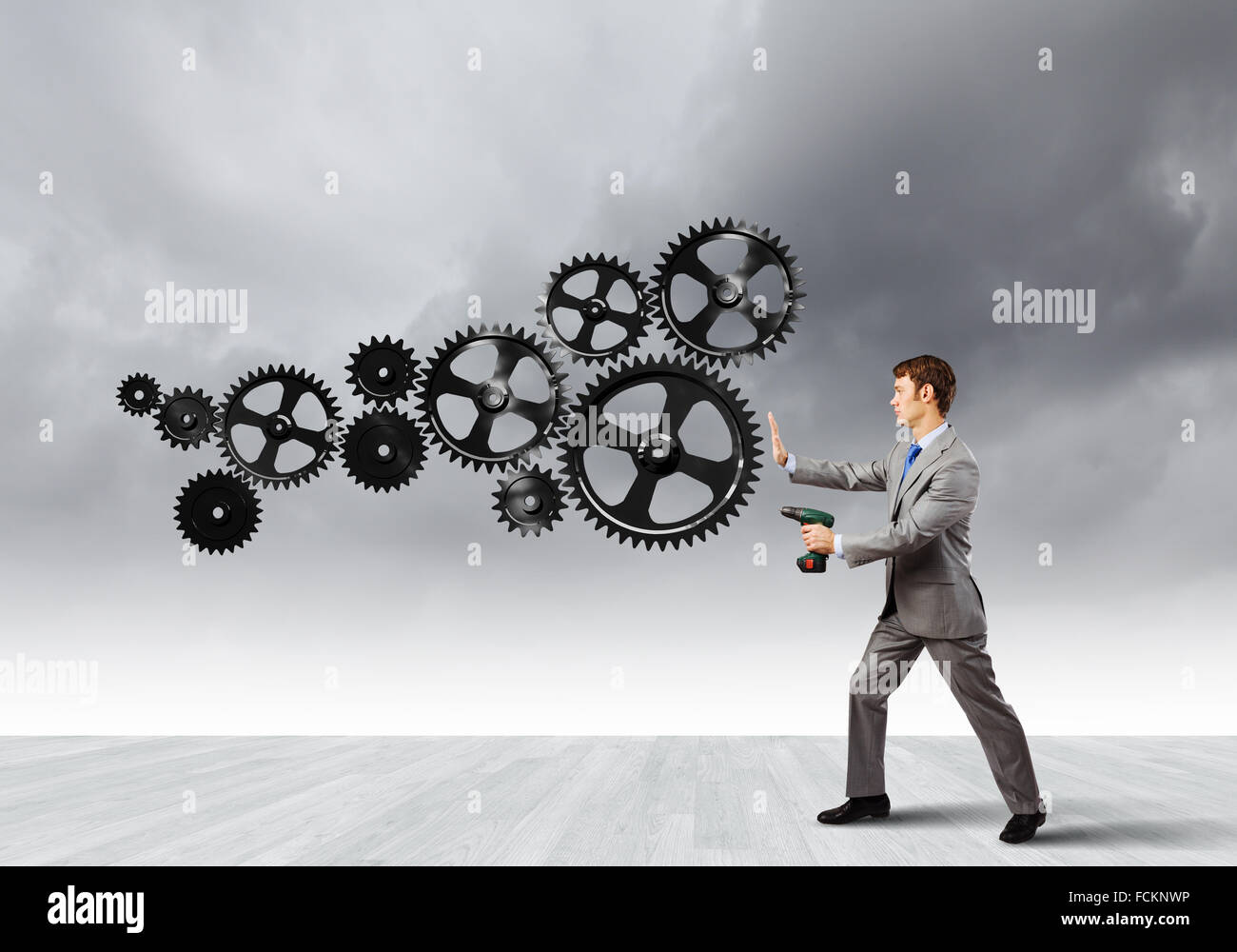 Young businessman using drill to fix gear mechanism Stock Photo - Alamy