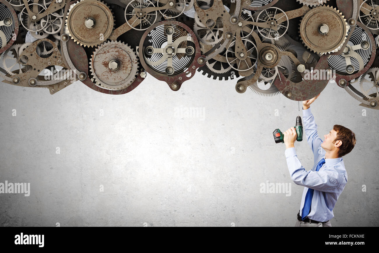 Young businessman using drill to fix gear mechanism Stock Photo - Alamy