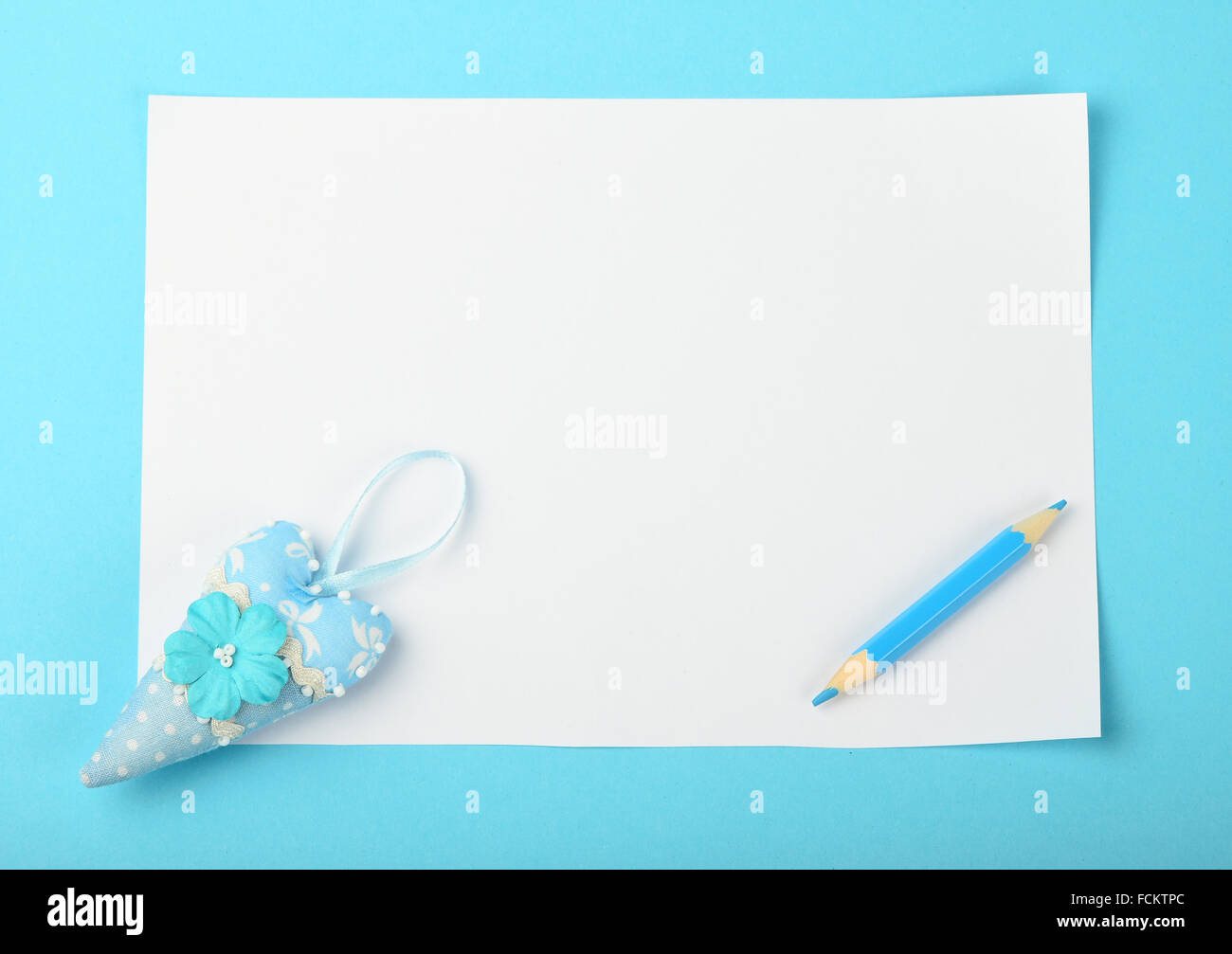 White paper note with tiny textile toy heart and small pencil on tender ...