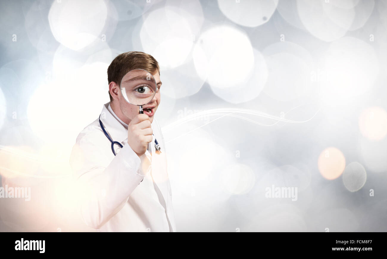 Funny young doctor with magnifier expecting something Stock Photo - Alamy