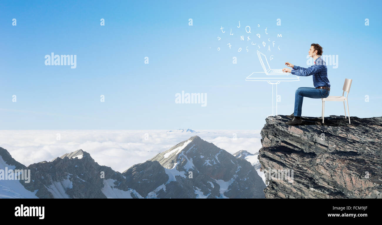 Young man sitting in chair on top of rock and using laptop Stock Photo ...
