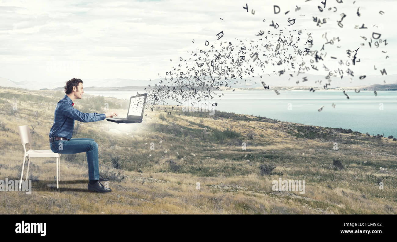 Young man sitting in chair and using laptop Stock Photo - Alamy