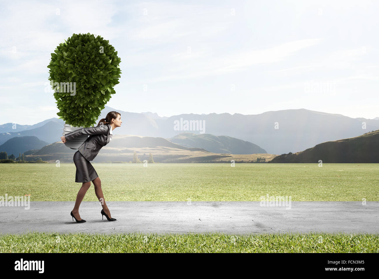 Young businesswoman carrying green light bulb on back Stock Photo - Alamy