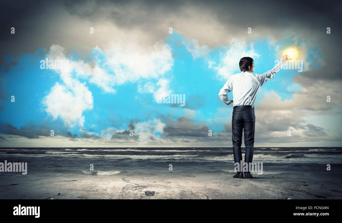 young man standing with back touching sun against clouds background ...