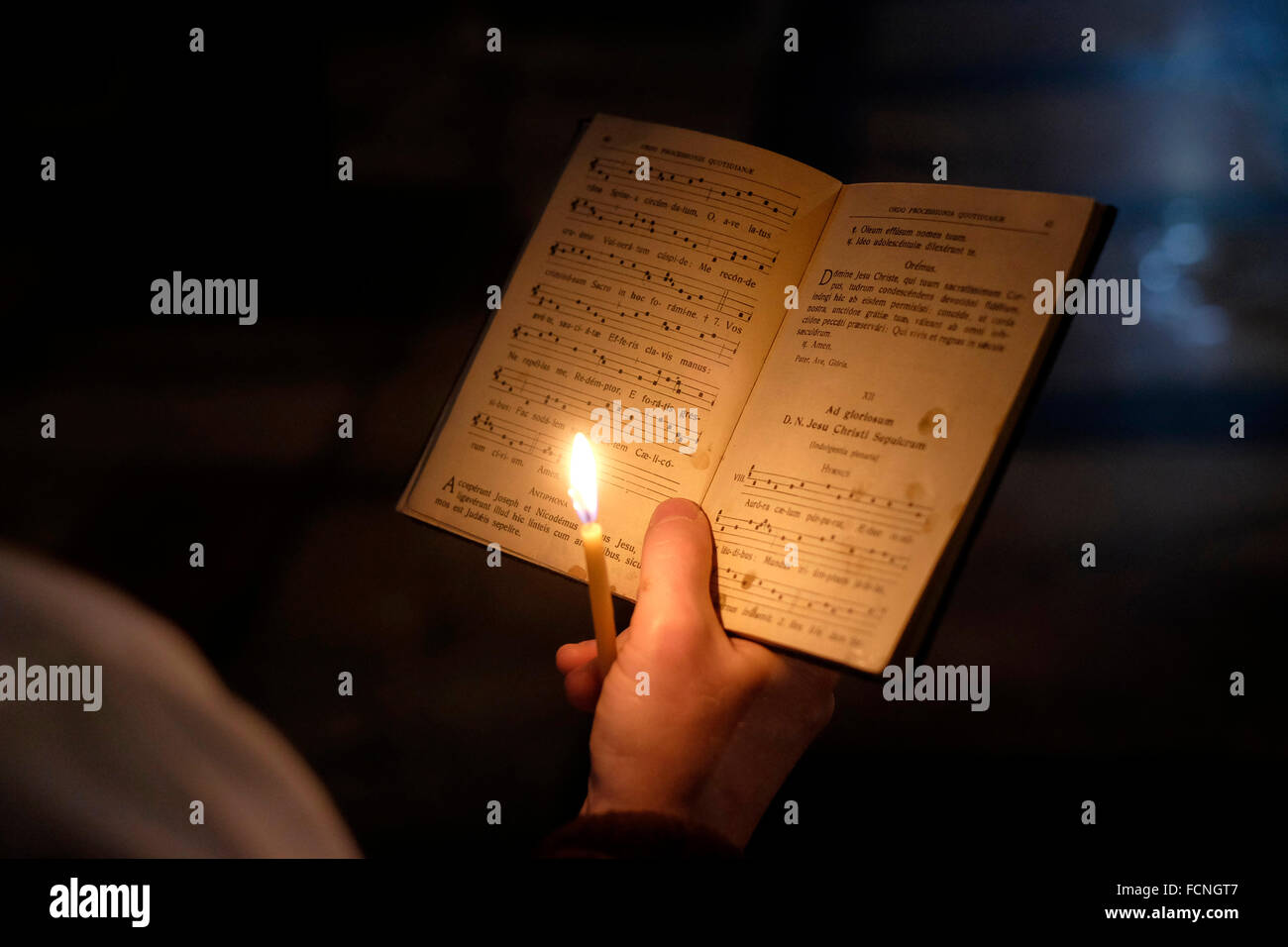 Christian Latin Catholic priest holds a candle and a hymnal book as he ...