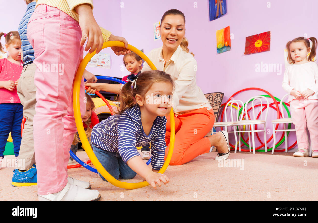 Kids crawl though hoop with teacher and friends Stock Photo - Alamy