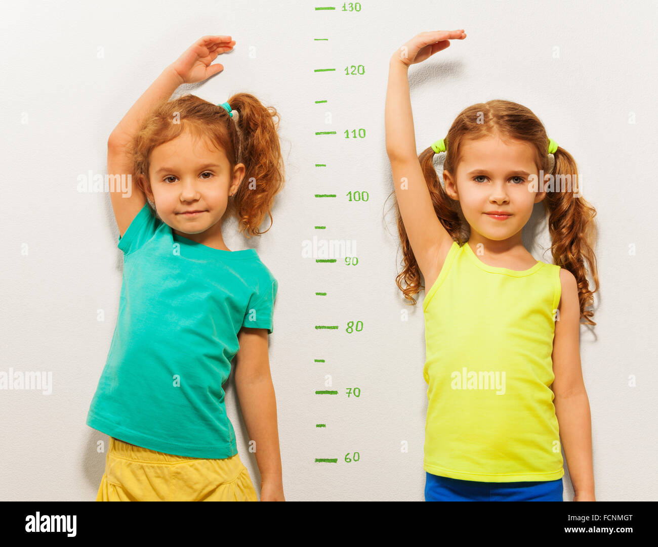 Two girls show height on wall scale at home Stock Photo - Alamy