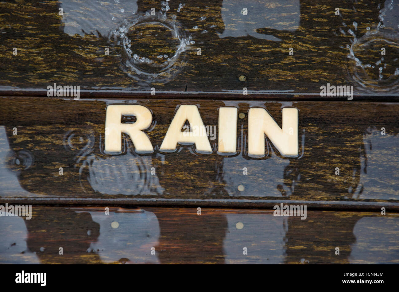 Letters forming the word rain laid on a outside timber deck in the rain ...