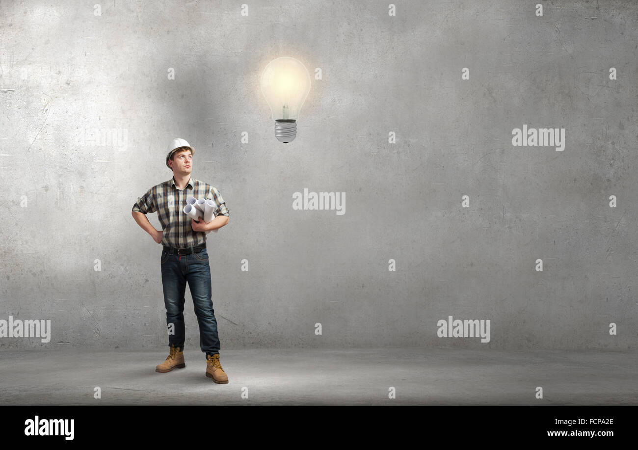 Young man builder looking thoughtfully at light bulb. Idea concept ...