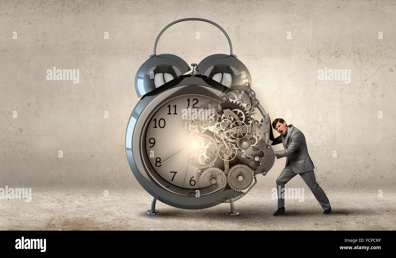 Businessman making effort to move alarm clock Stock Photo - Alamy