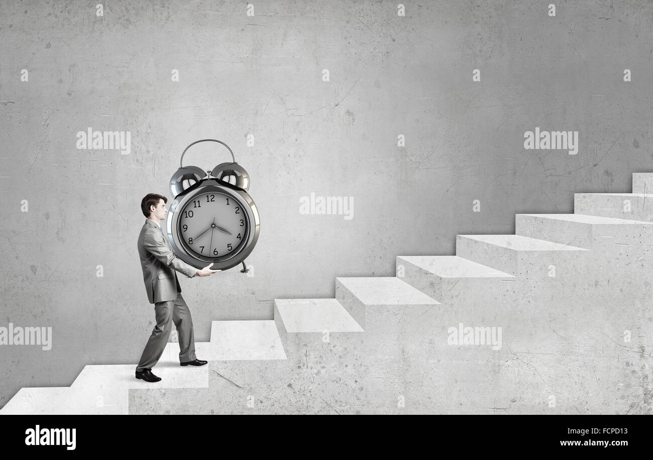 Young businessman carrying with effort huge alarm clock Stock Photo - Alamy
